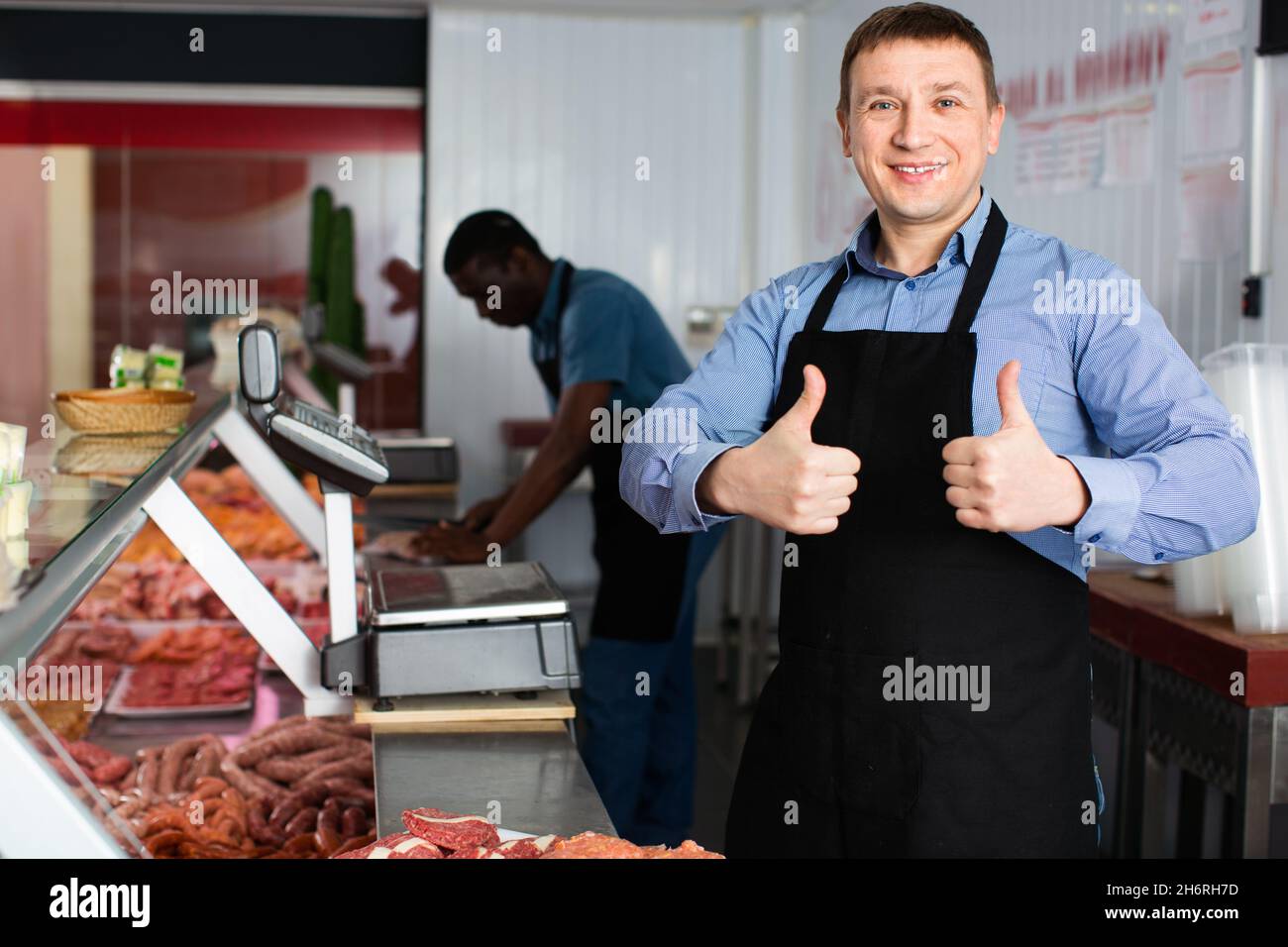 Proud male owner of butcher shop standing behind counter, giving thumbs ...