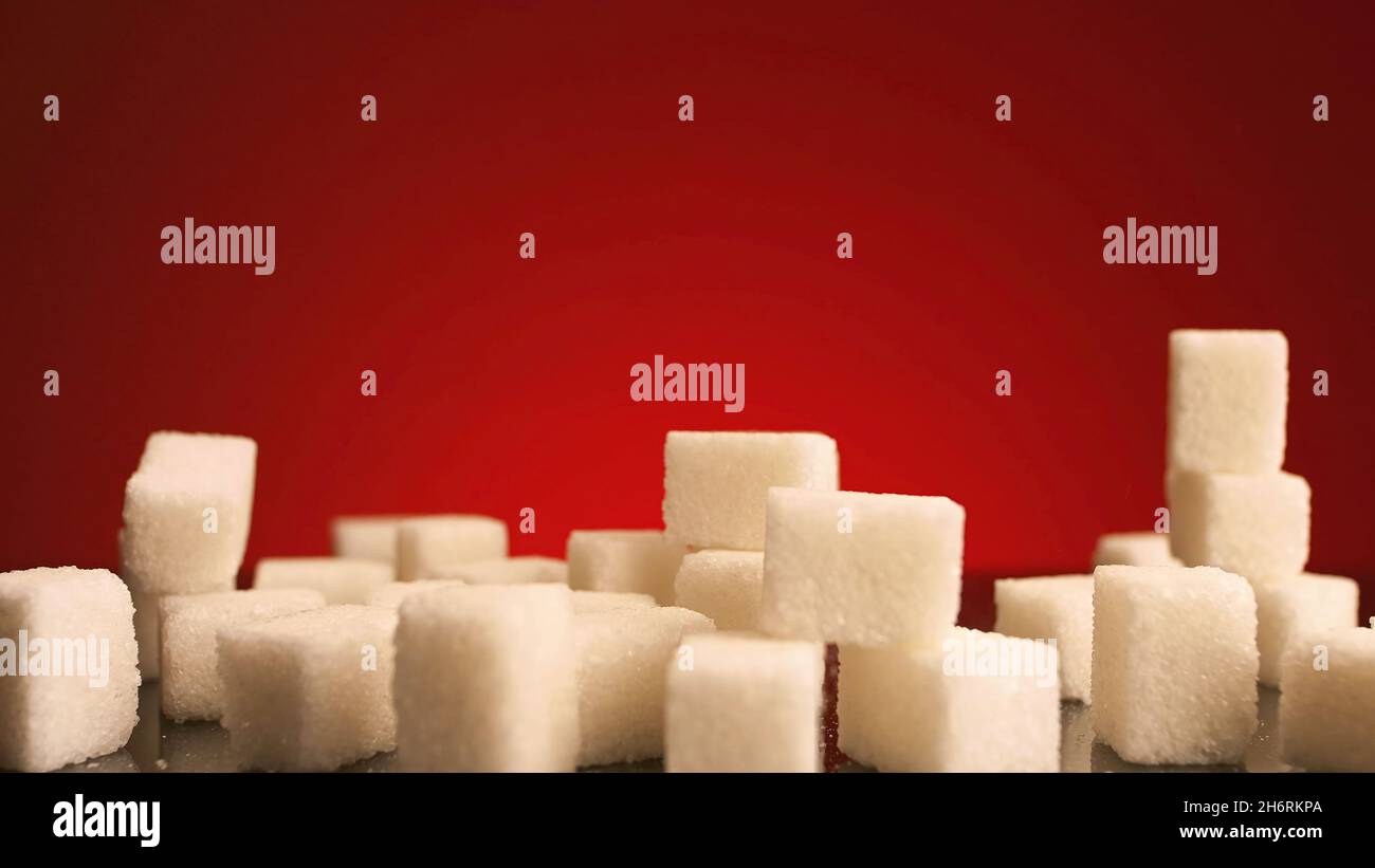 Close up of small sugar cubes falling down isolated on red background ...