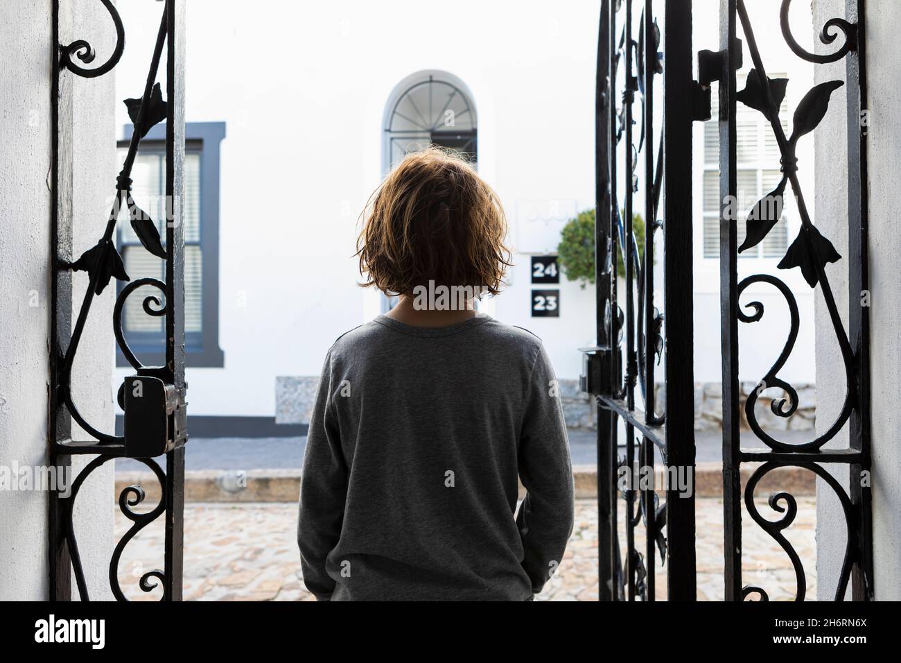 A boy standing looking out of open ironwork gates Stock Photo - Alamy