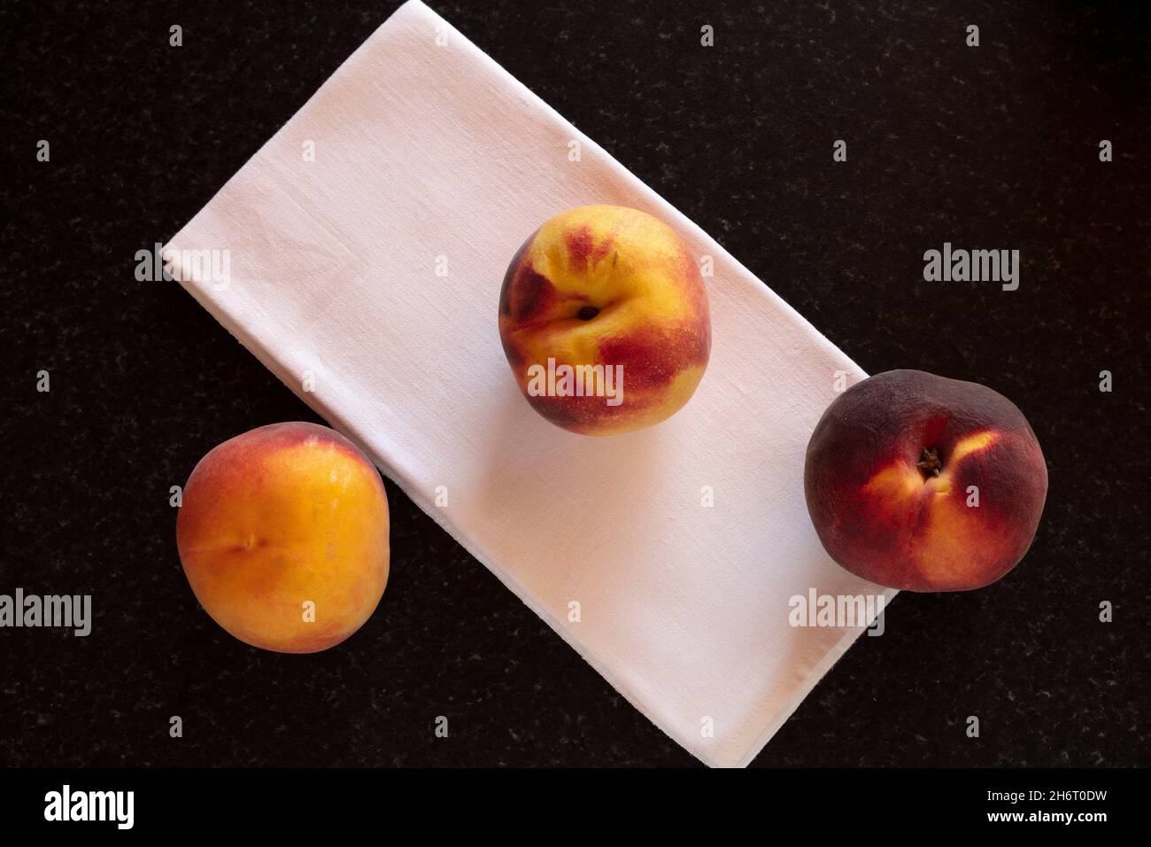 Three peaches (Prunus persica) and white napkin on plain background ...