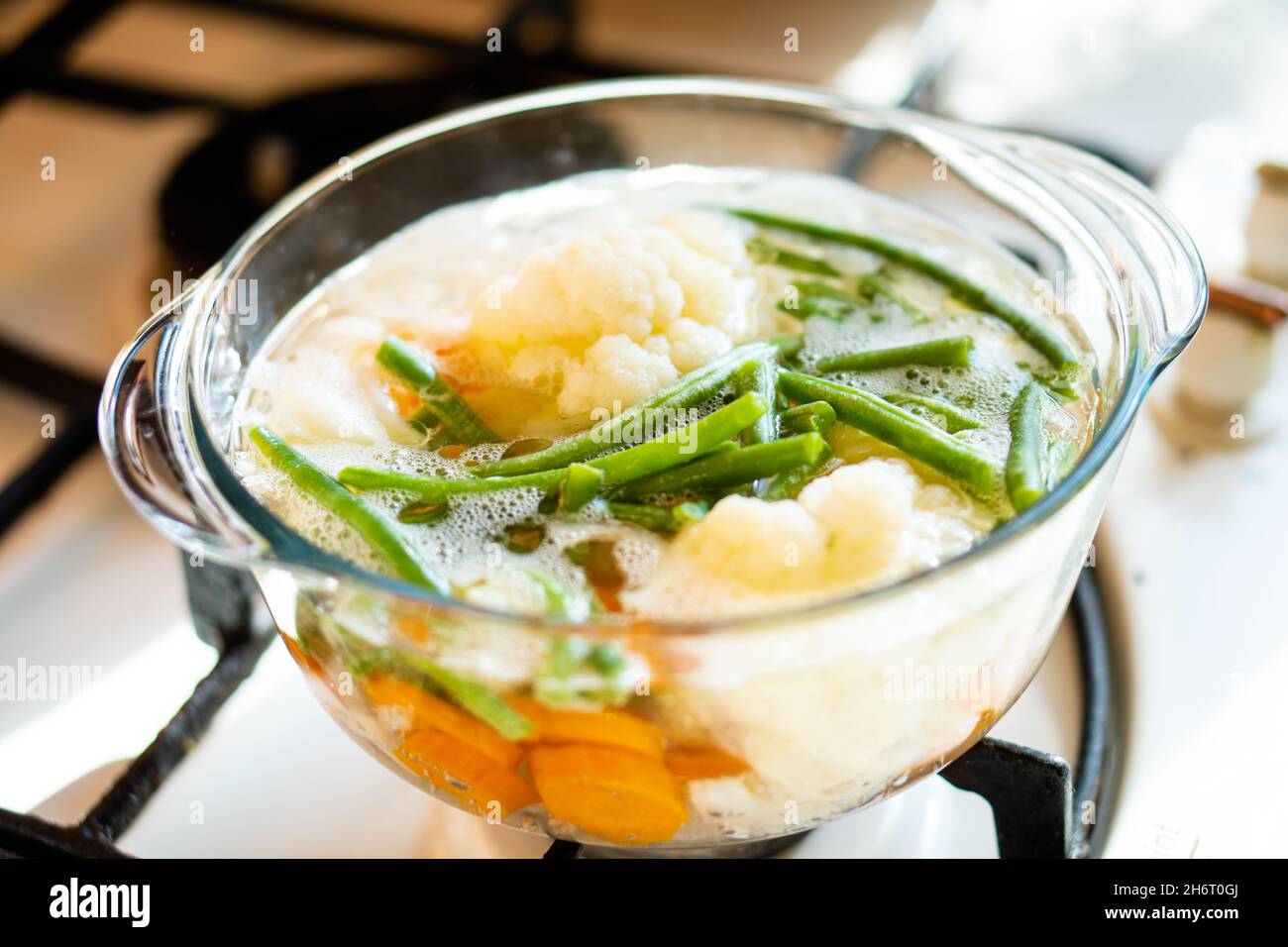 Transparent glass pan with vegetable soup, fresh hot food boils on the ...