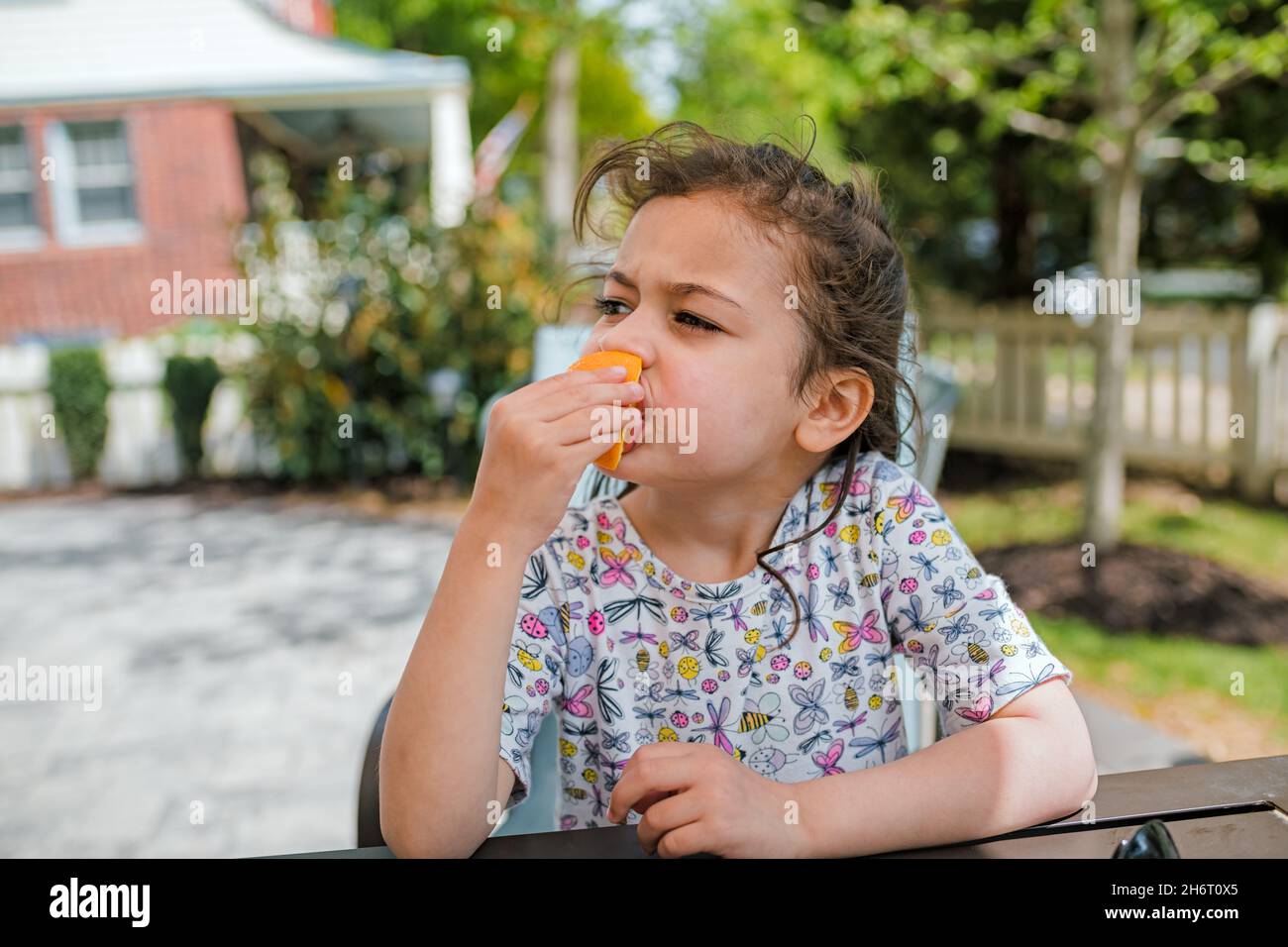 Young girl eating orange slice sitting outside Stock Photo - Alamy