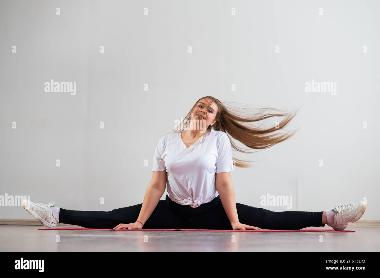 A young flexible fat woman sits in a transverse twine and waves her ...