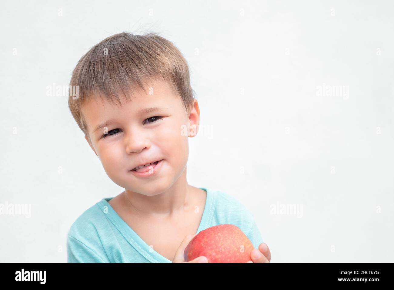 The child is eating an apple on a gray background. Boy licks his lips ...