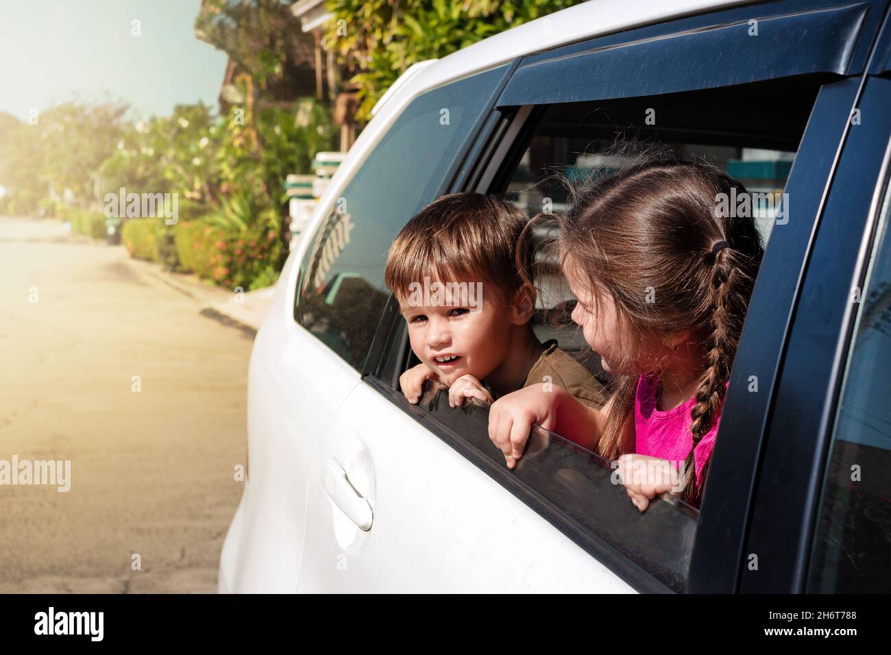children lean out of the car window and look at the street. a boy and a ...