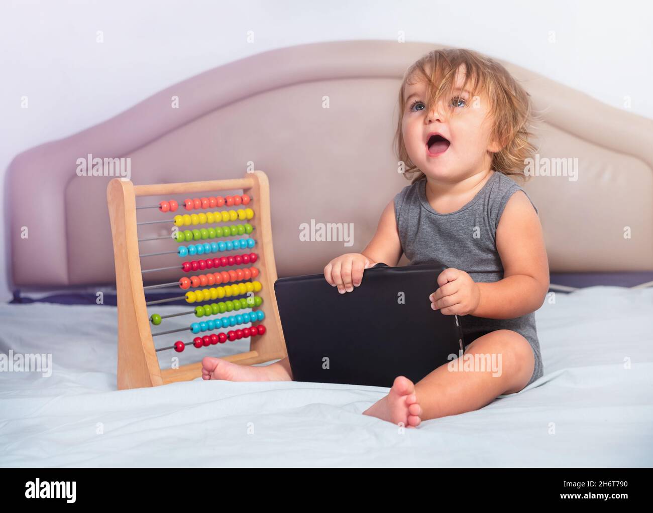The baby sits on the bed with a tablet and bills. Skills development ...