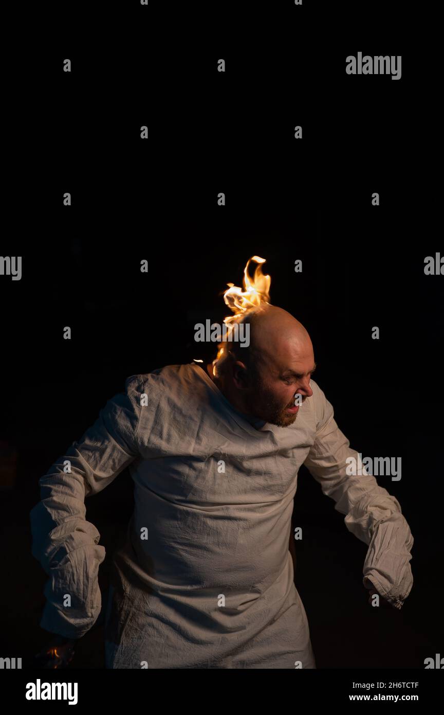 Bald man in a straitjacket with a burning head on a dark background ...