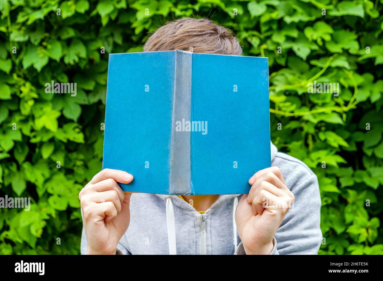Person hides the Face behind the Book on the Green Leaves Background ...