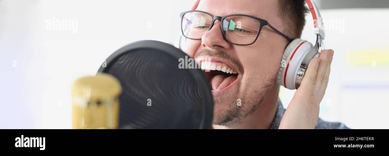Portrait of singing young man in headphones front of microphone in ...