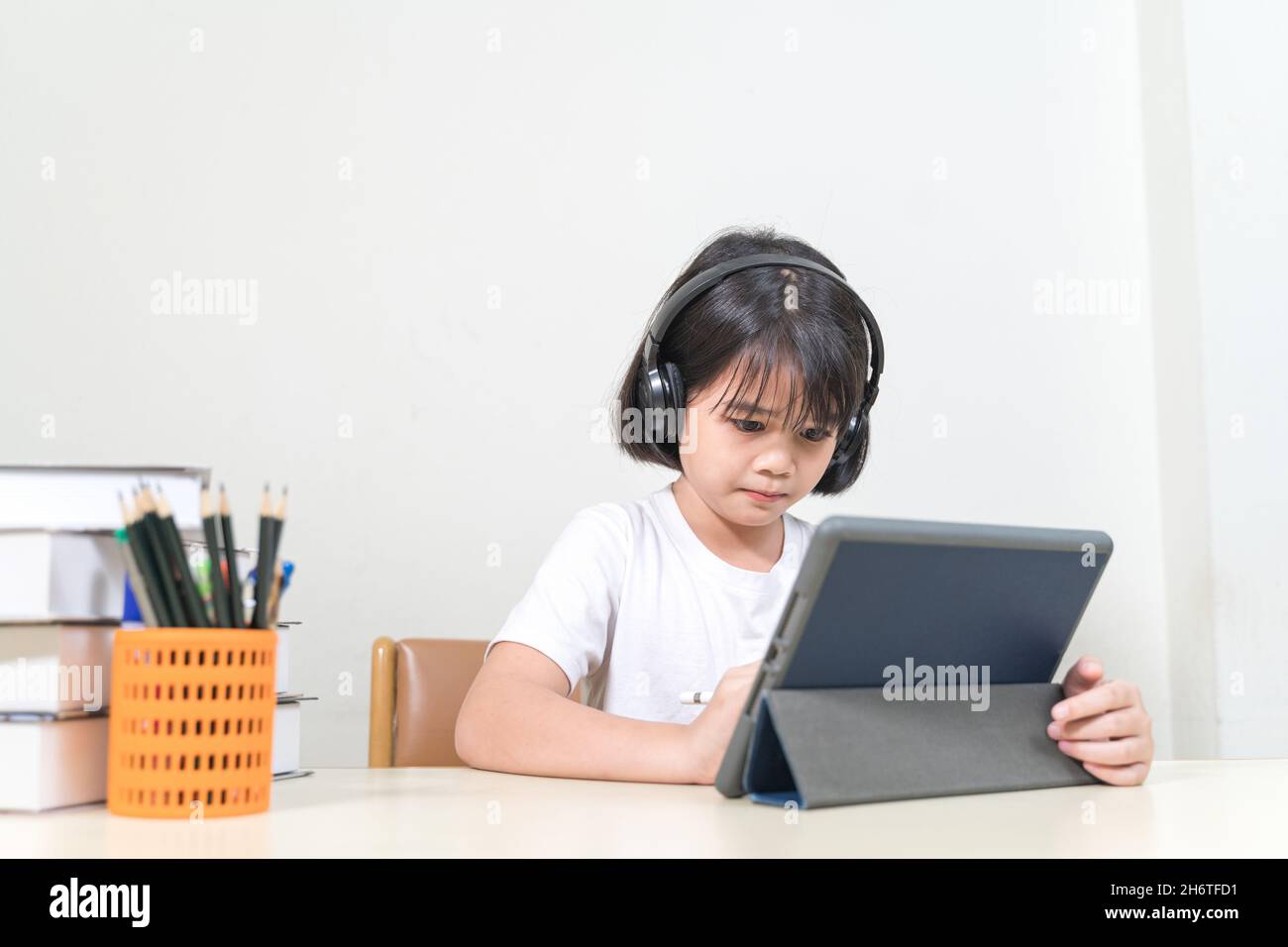Asian female kid wearing earphones and doing homework on a tablet -the ...