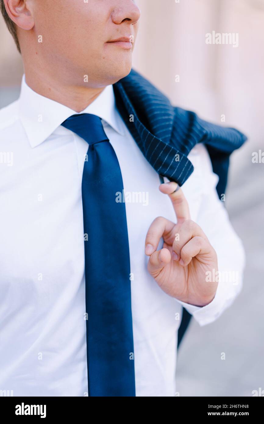 Man in a white shirt holds a jacket hanging on his shoulder with his ...