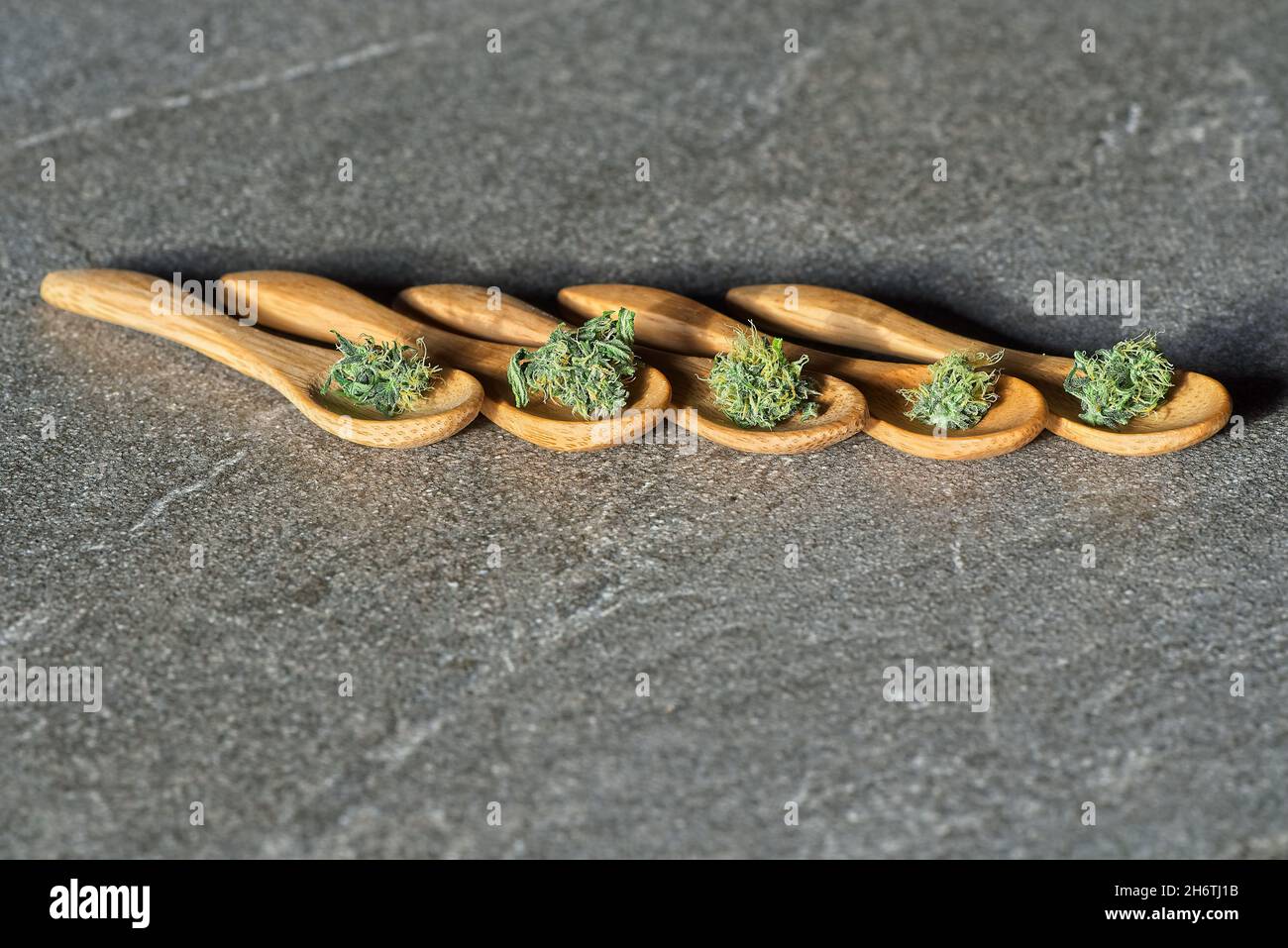 Small cannabis buds on little wooden bamboo spoons in line on grey ...