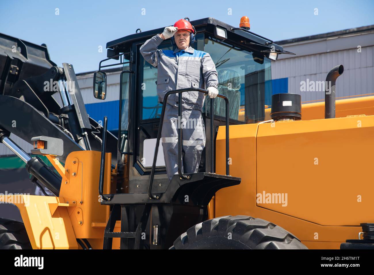 Excavator driver in hard hat stands at construction equipment, concept ...