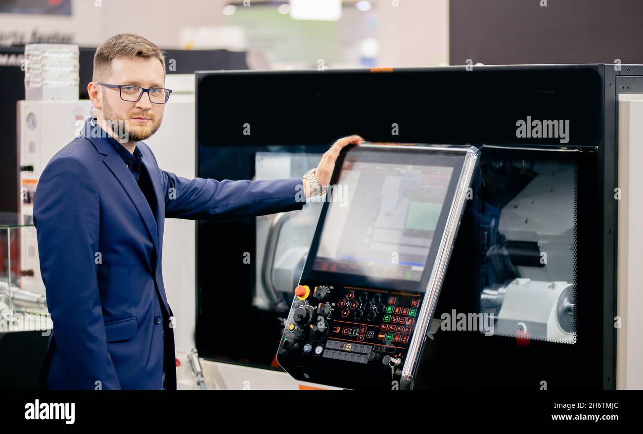 Engineer young man in glasses operates CNC automatic metalworking lathe ...