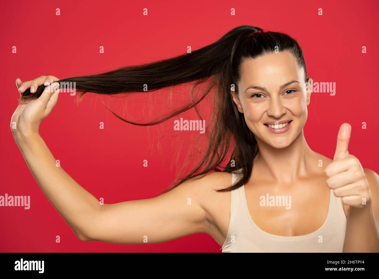 a young happy woman holds and shows her long hair and showing thumb up ...