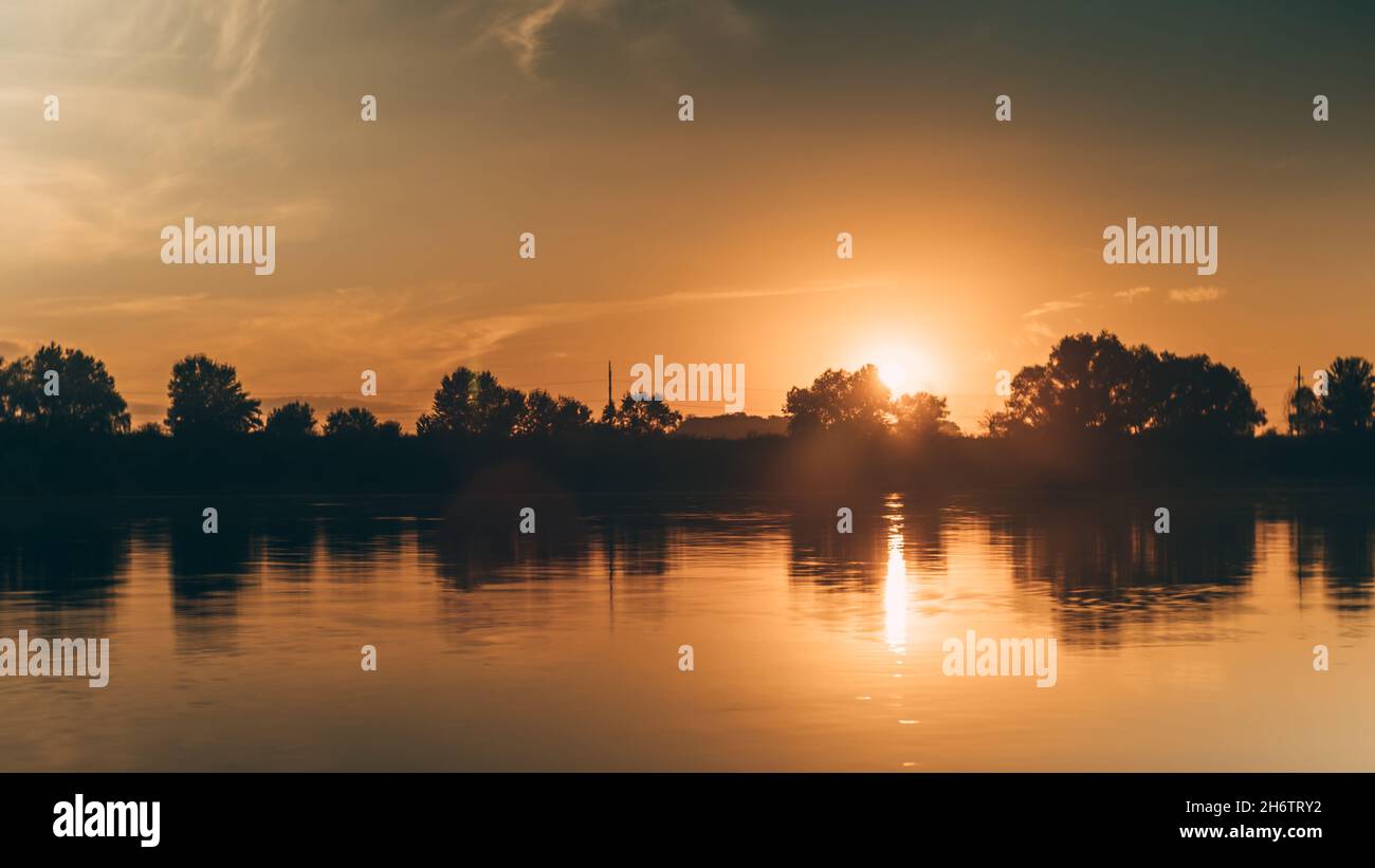 A warm orange sunset over the river. Trees and clouds reflected in the ...