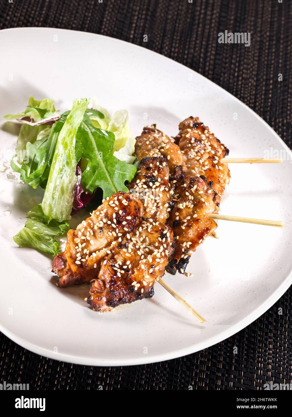 portion of grilled chicken wings skewers with mix salad on a plate on ...