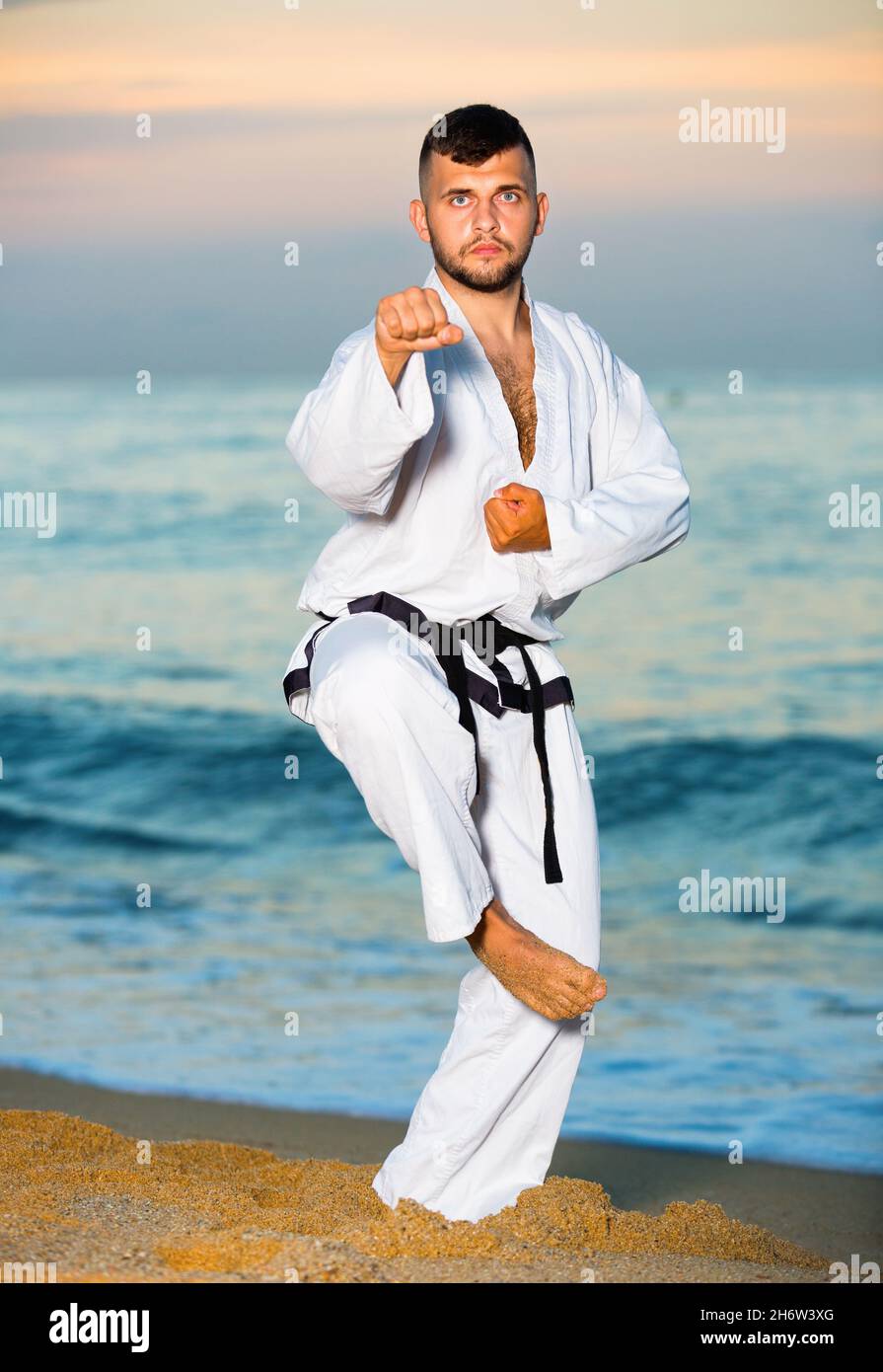 Man in uniform doing taekwondo exercises at sunset sea shore Stock ...