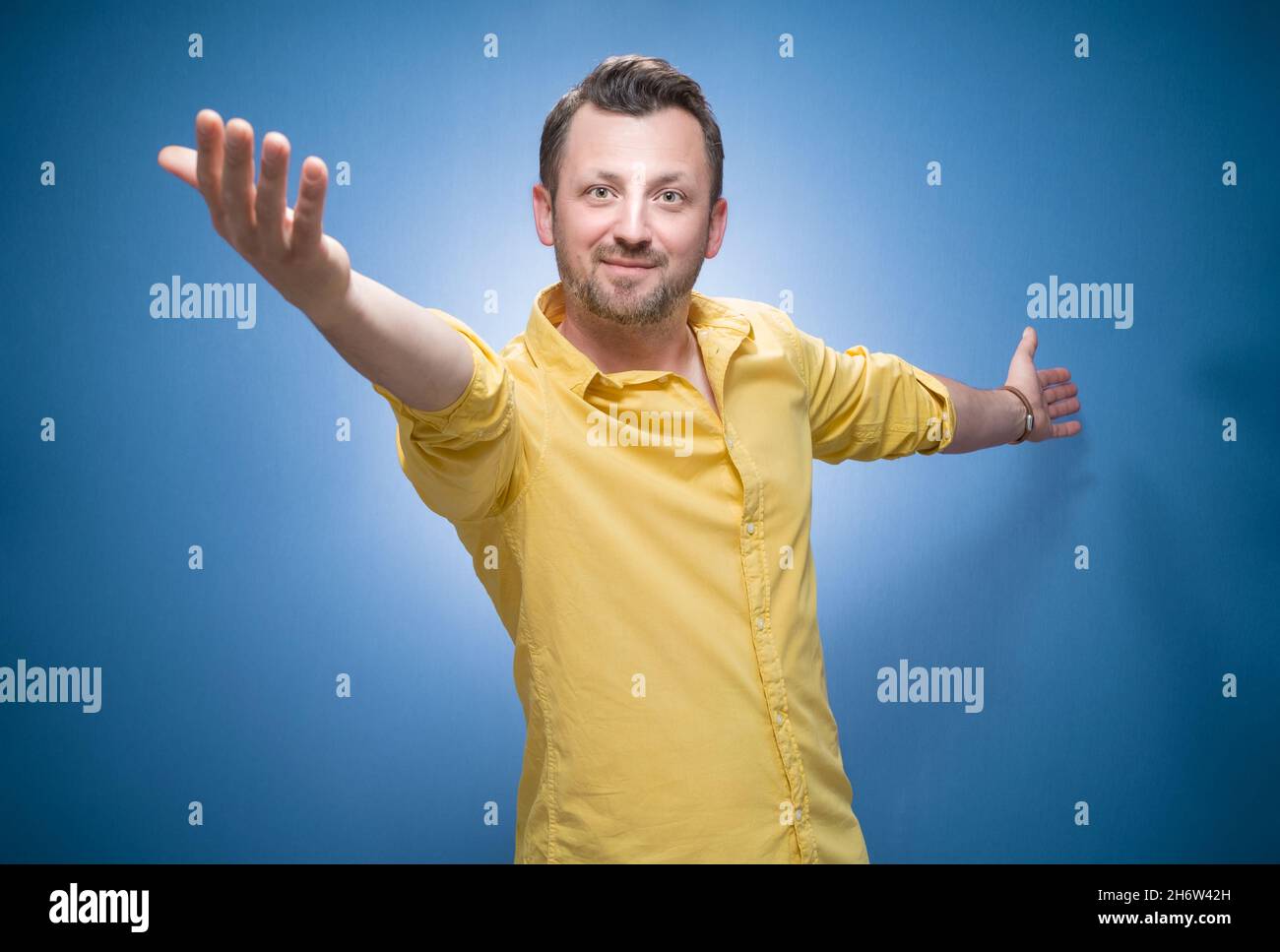 Friendly young man with wide open arms, welcome concept over blue ...