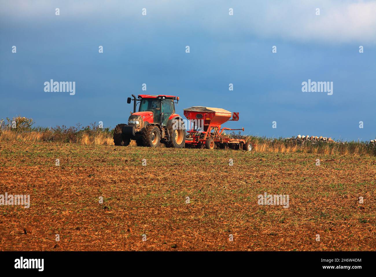A large red Tractor running around the field sowing the seeds for ...