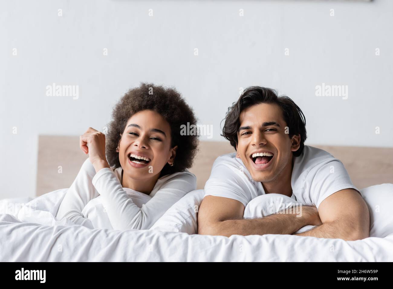 happy multiethnic couple laughing while lying in bed Stock Photo - Alamy