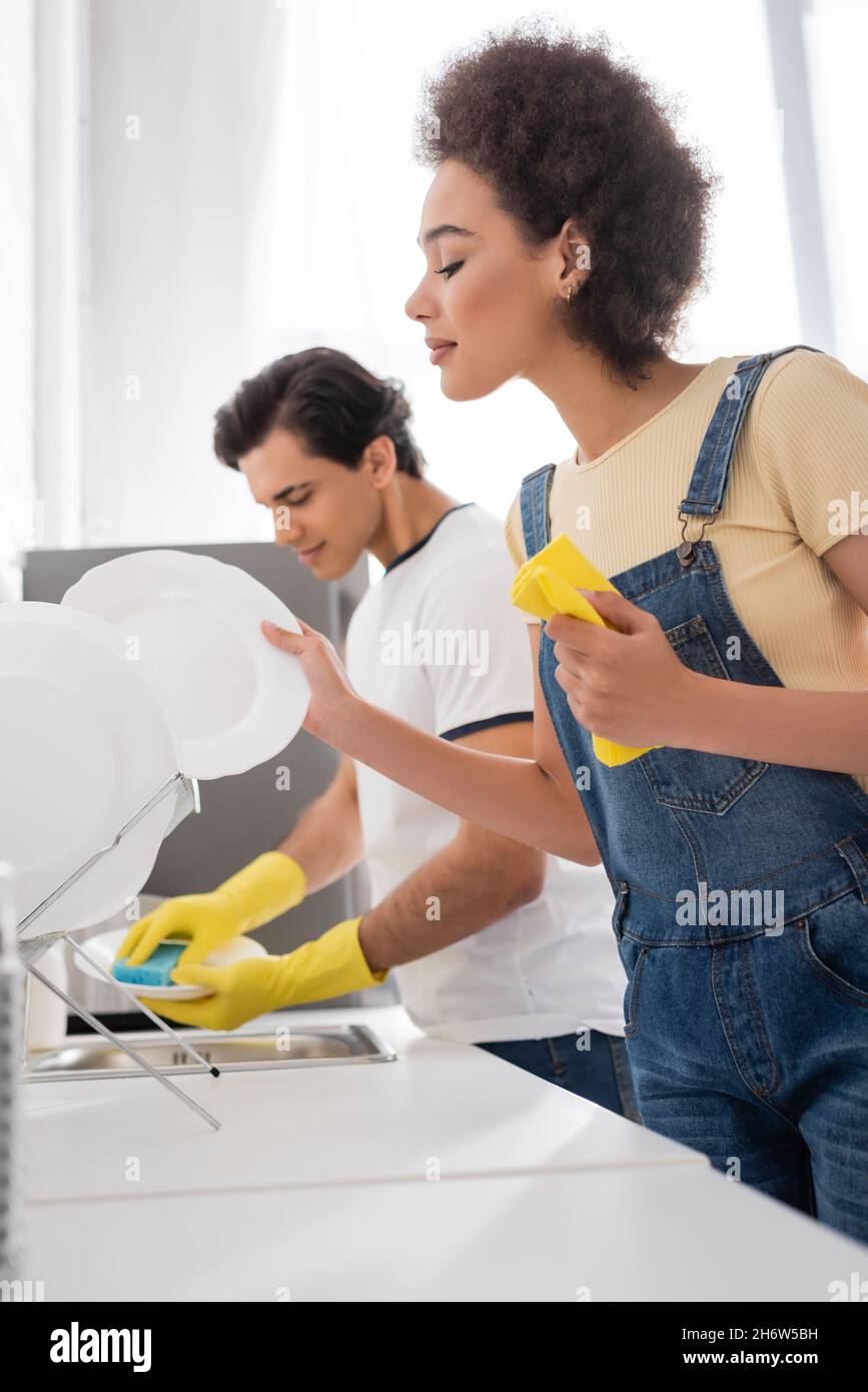 smiling african american woman holding plate and rag near blurred ...