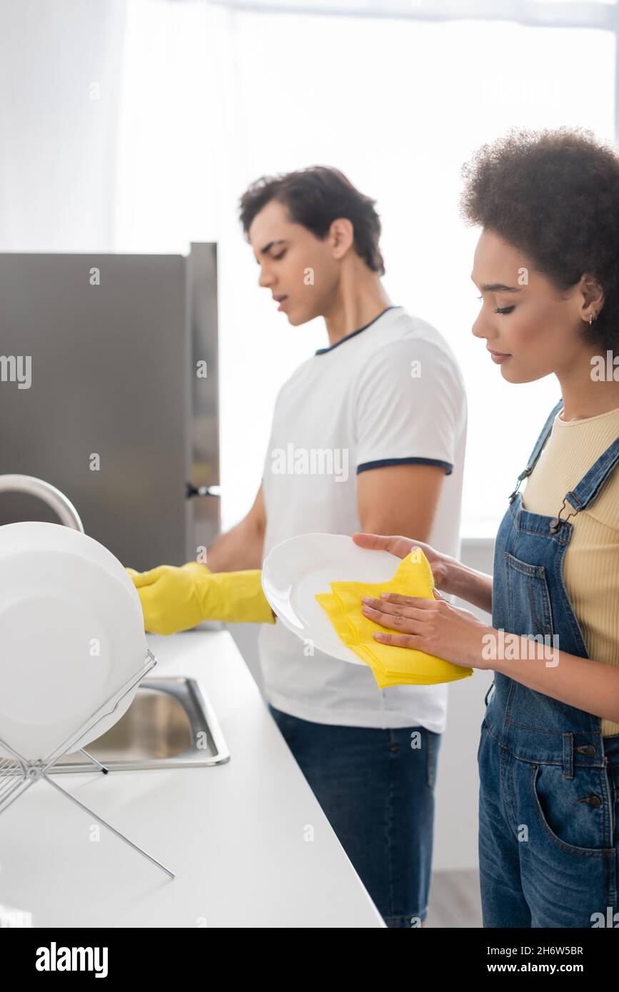 curly african american woman cleaning plate with rag near blurred ...