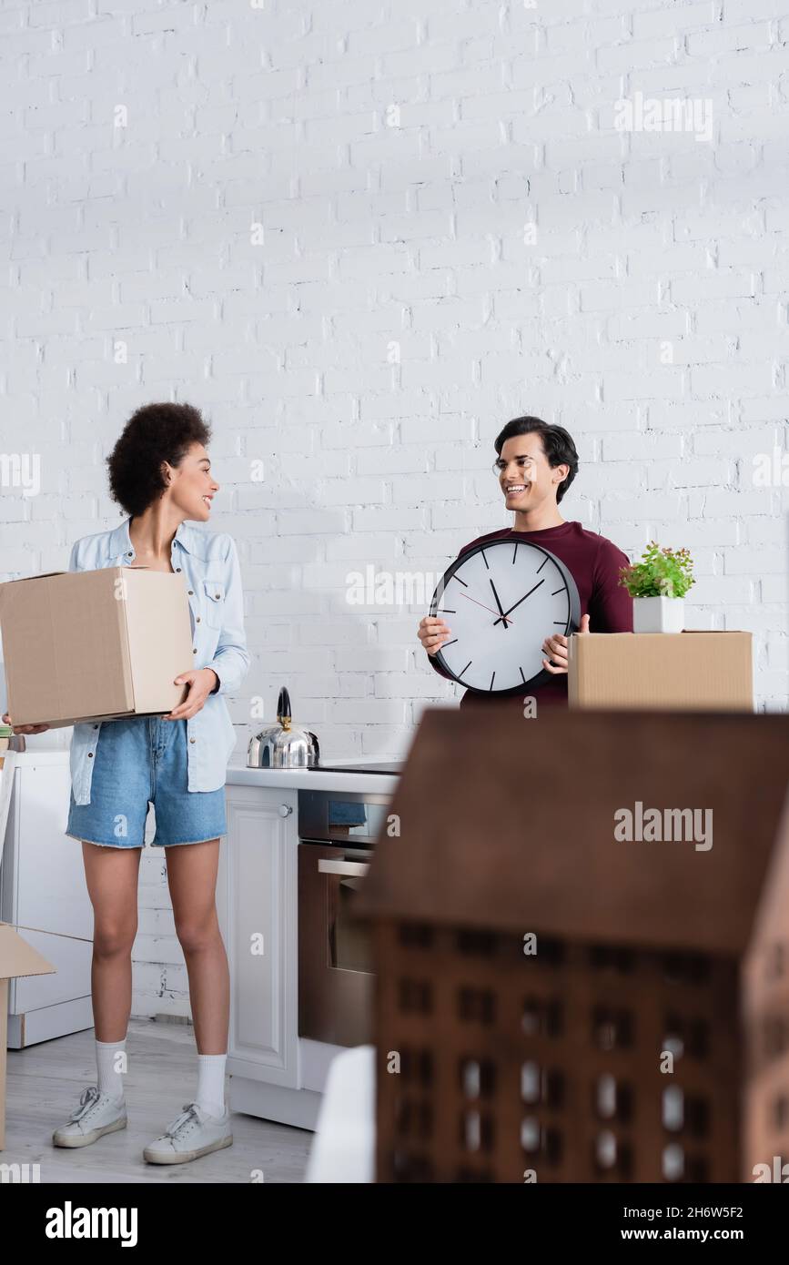 happy man holding wall clock near african american girlfriend with ...