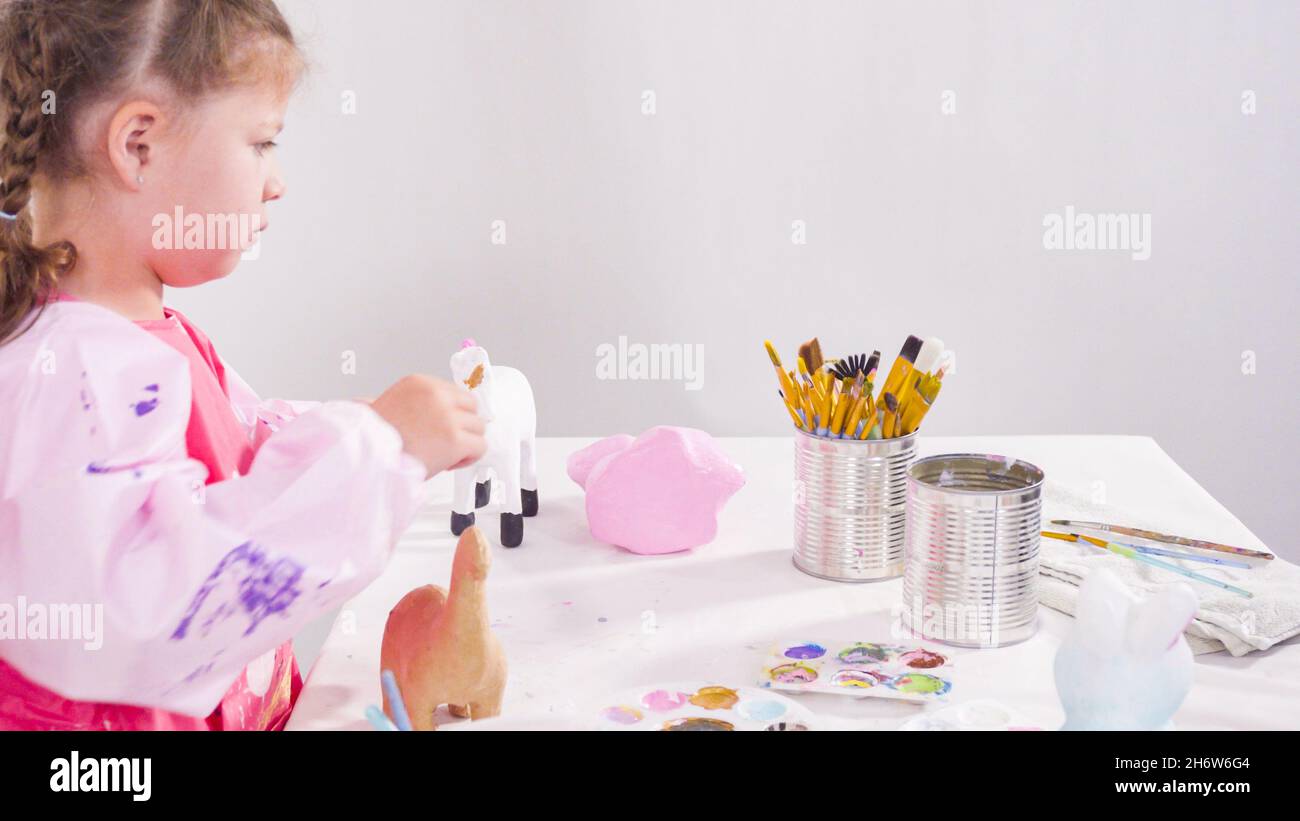 Little girl painting paper mache figurines with acrylic paint for her ...