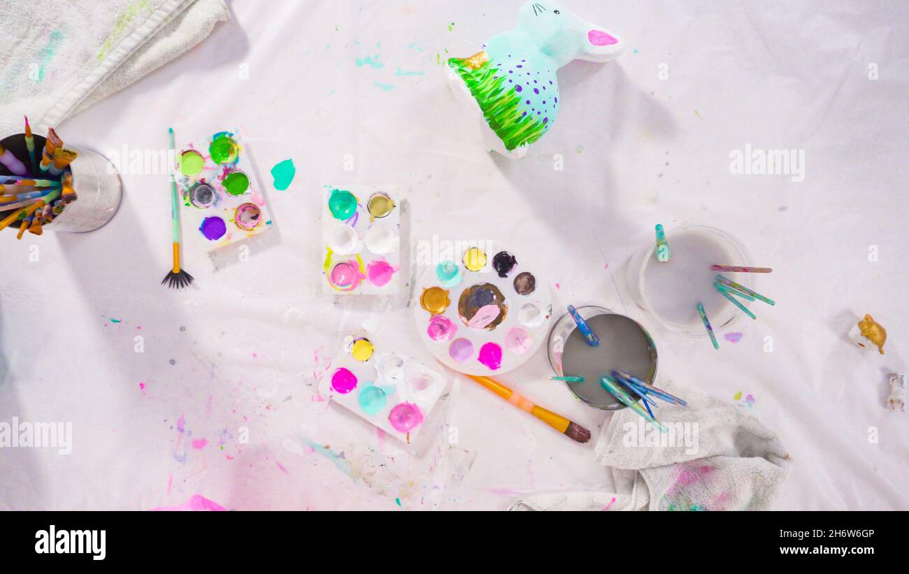 Flat lay. Little girl painting paper mache figurines with acrylic paint ...