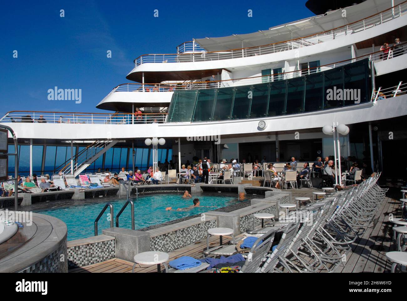 Passengers relaxing in the sunshine by the swimming pool midships on a ...
