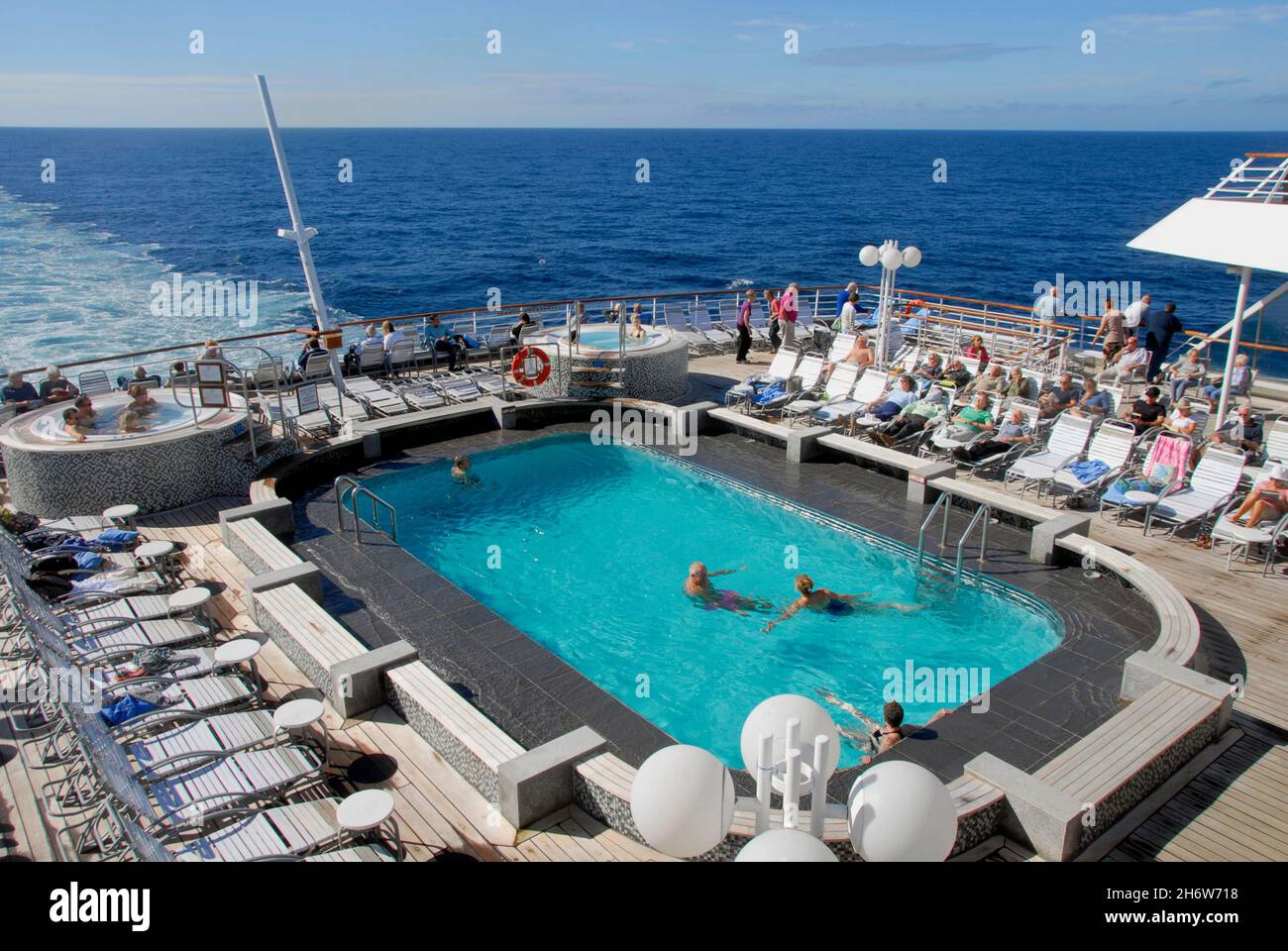 Passengers relaxing in the sunshine by the swimming pool on a cruise ...