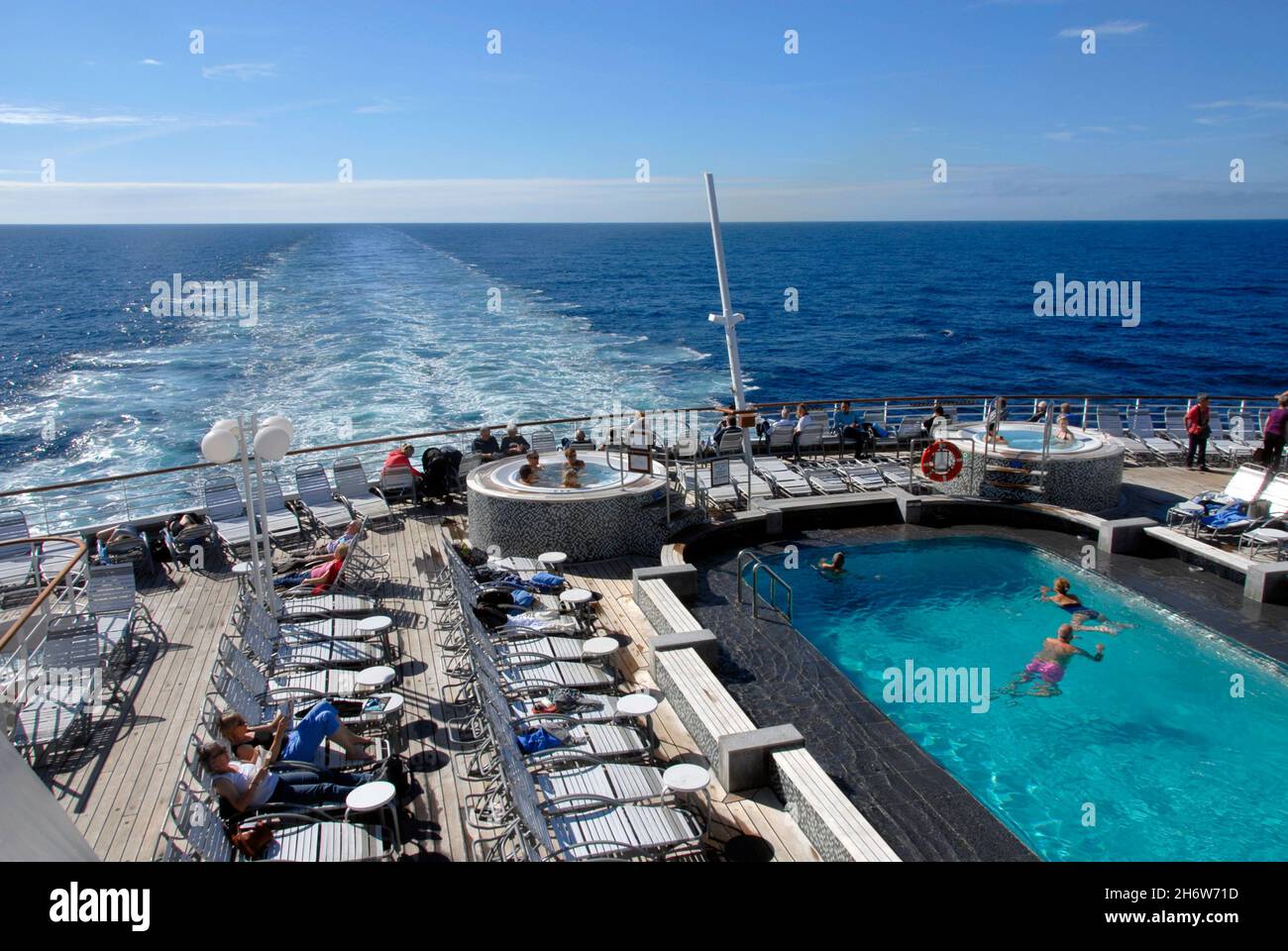 Passengers relaxing in the sunshine by the swimming pool on a cruise ...