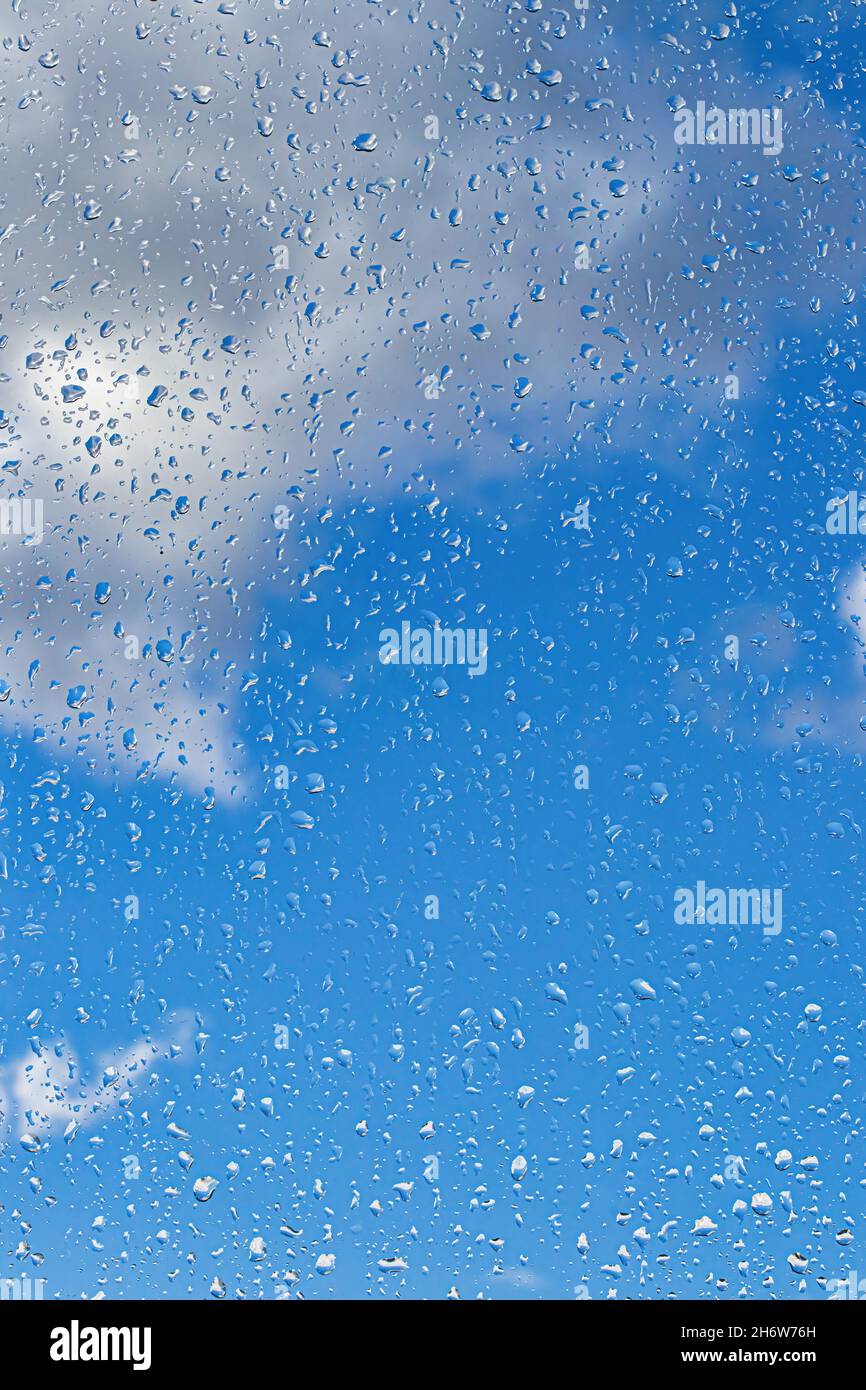 Rain drops on window glasses surface with blue sky and clouds ...