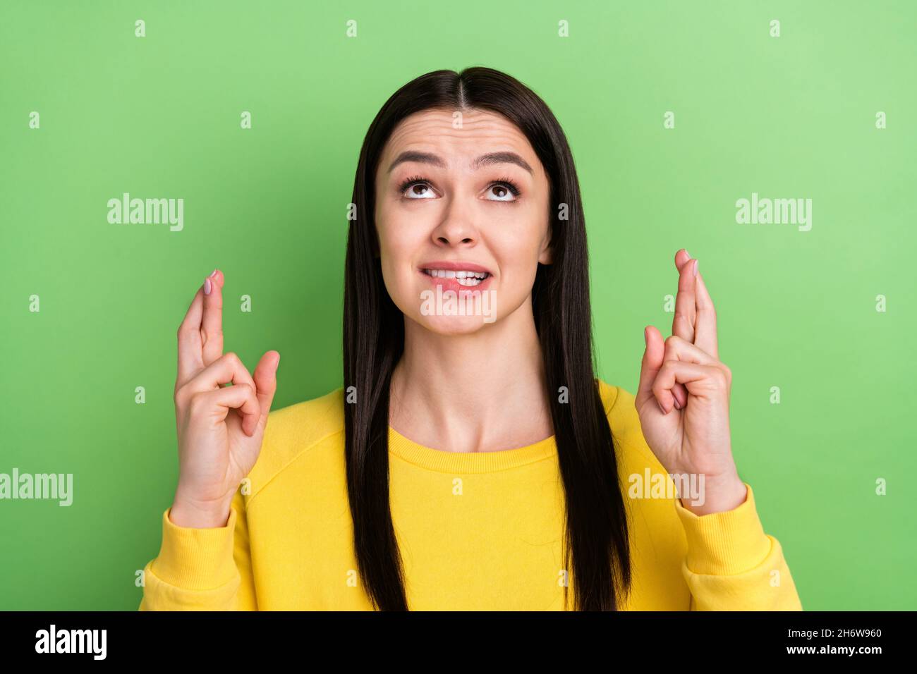 Photo portrait of woman biting lips with crossed fingers looking ...