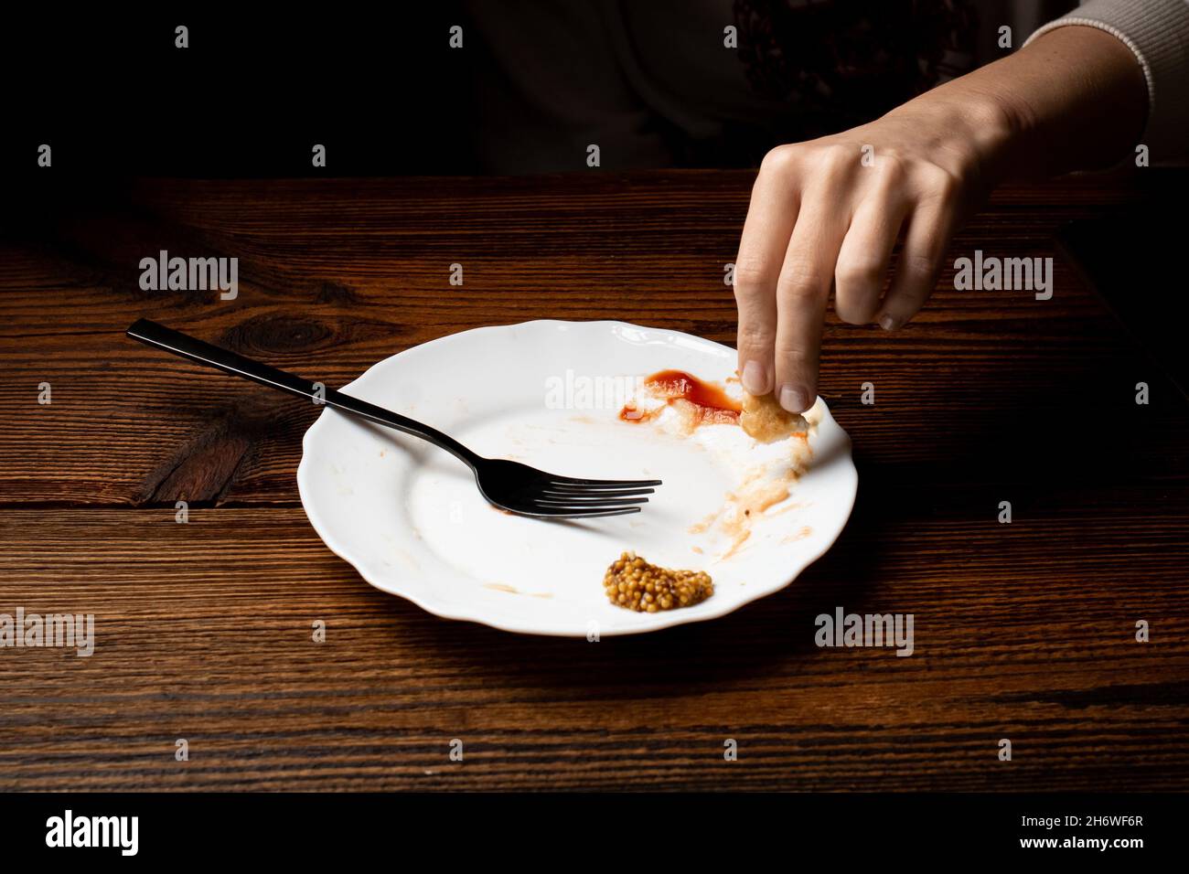 A woman eats food from a white plate in a dark room. Poverty, last meal ...