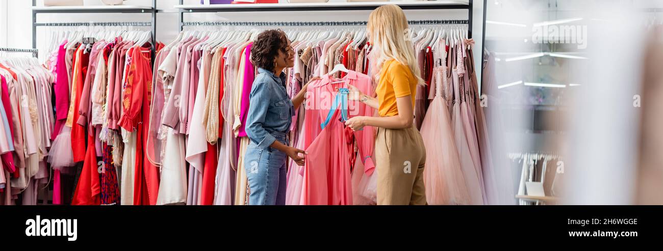 happy african american shop assistant showing pink dress to blonde and ...
