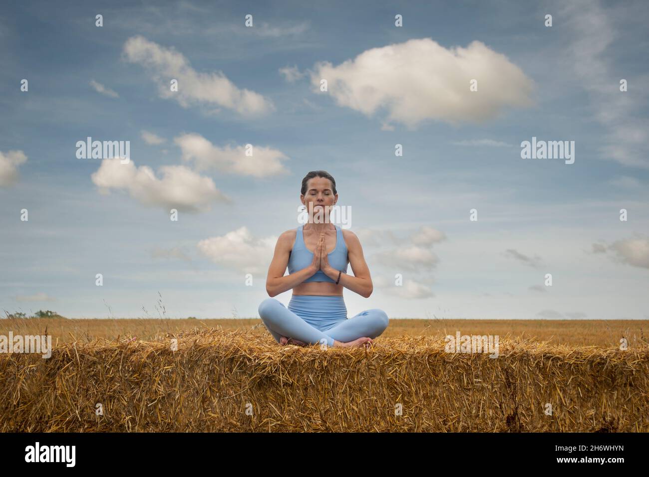 Fit woman sitting on a straw bale in the countryside sitting practicing ...