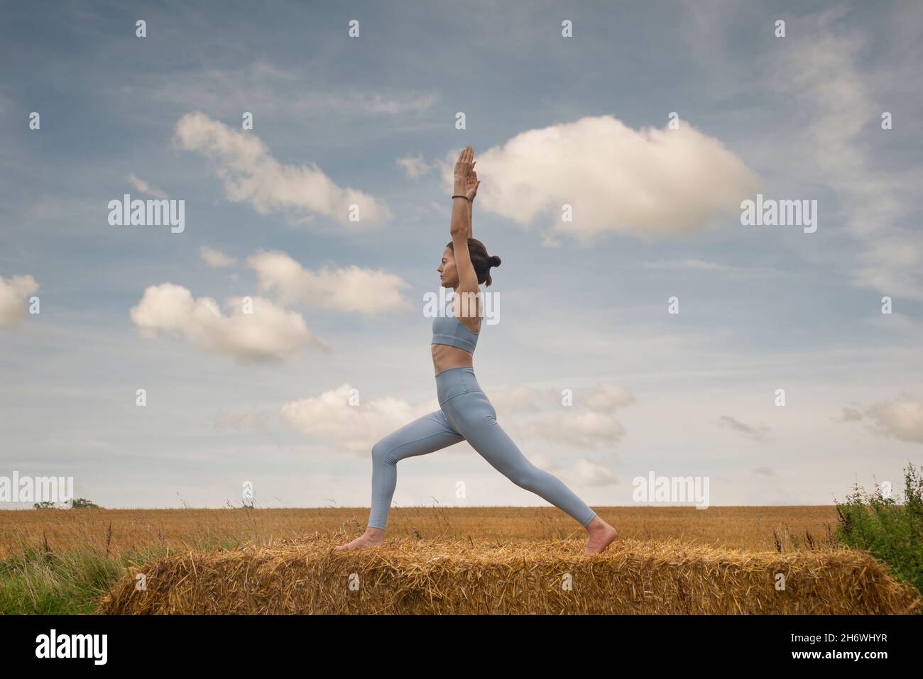 Woman practicing yoga and exercising in a field on a straw bale ...