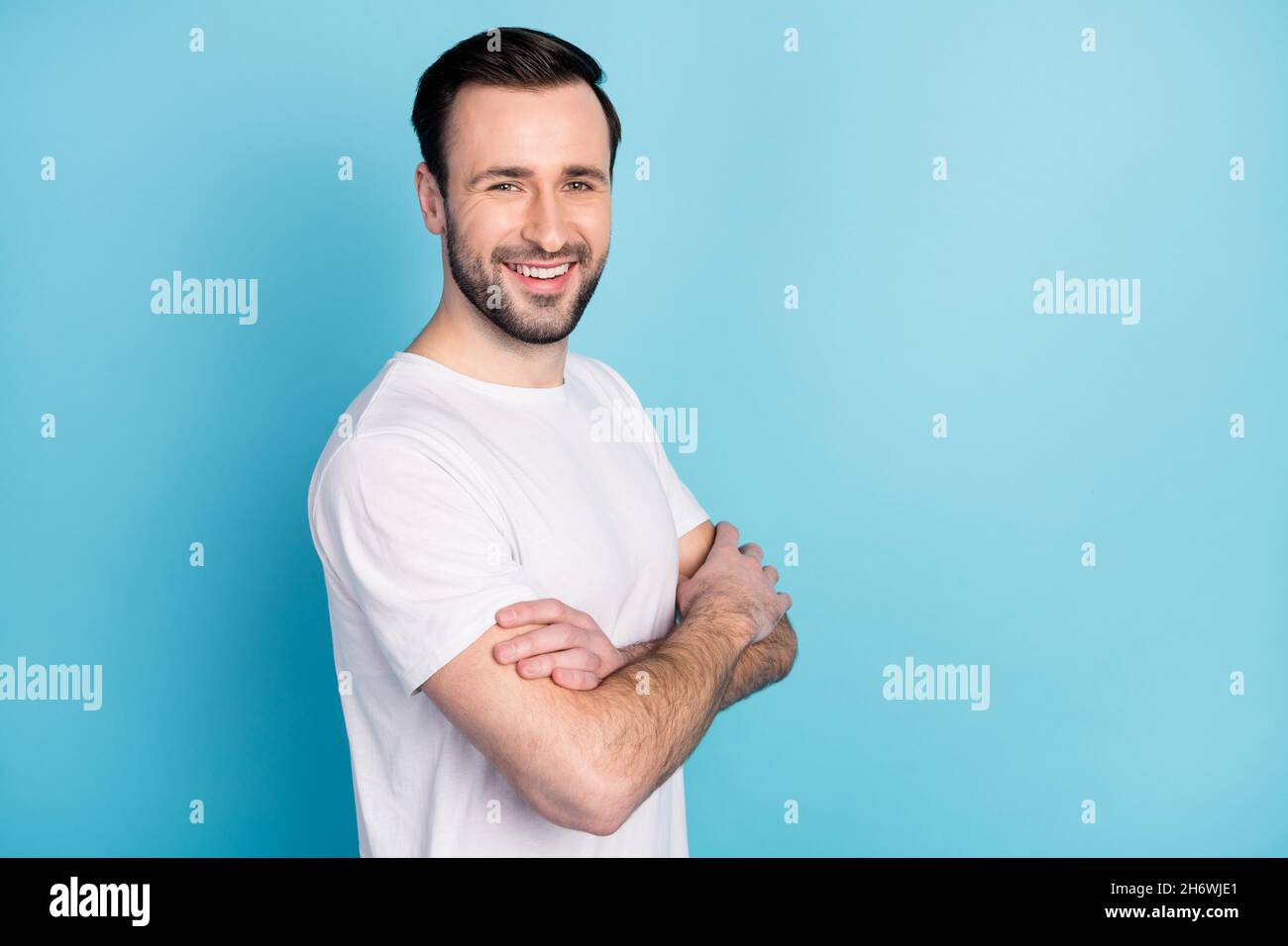 Profile photo of half turned satisfied glad man crossed arms beaming smile isolated on blue ...