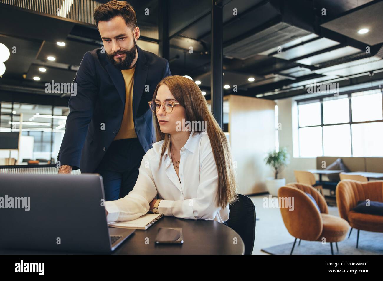 Two businesspeople having a discussion while working with a laptop in ... Two businesspeople having a discussion while working with a laptop in ...