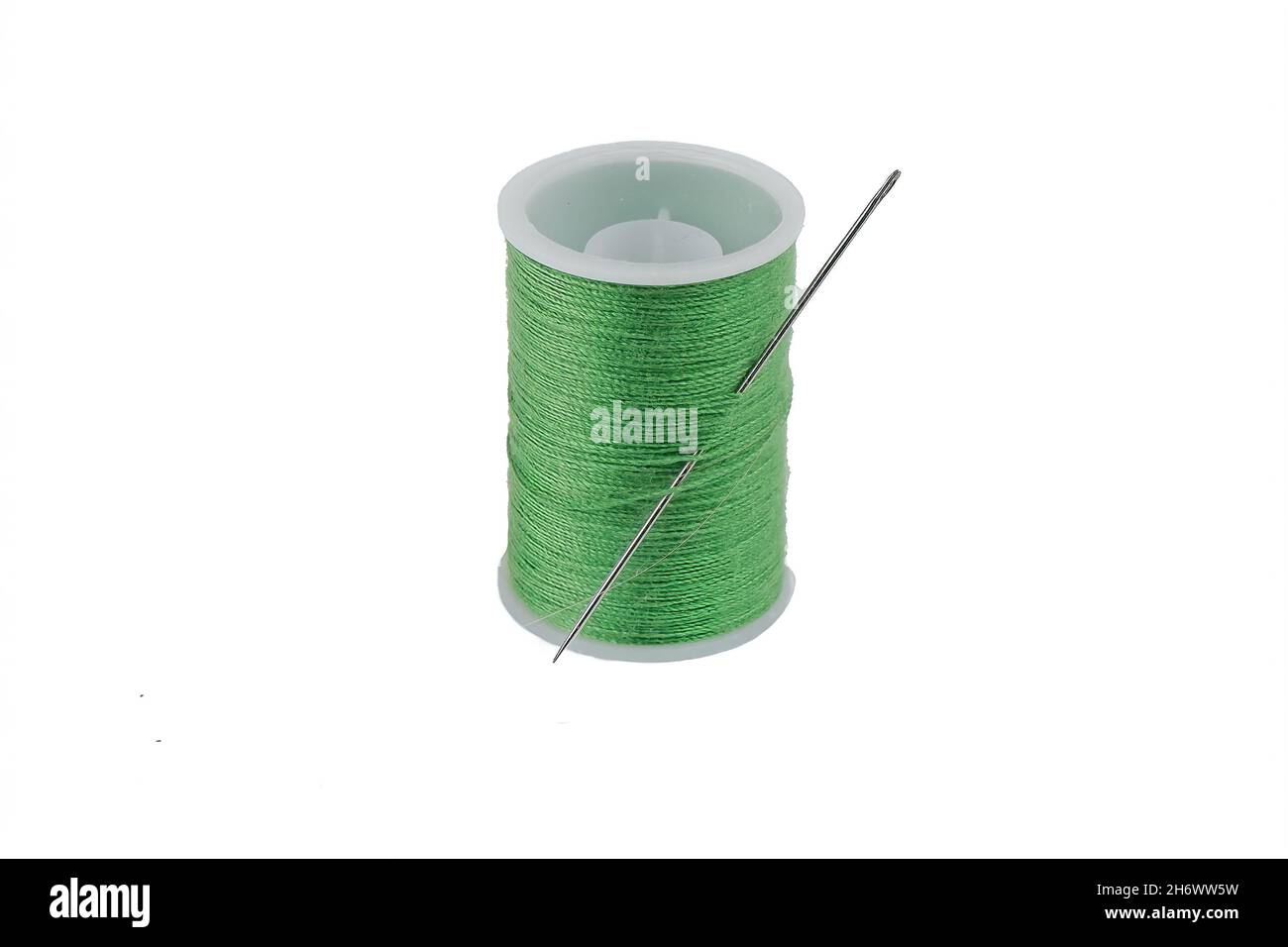a spool of green threads with a needle stuck in them isolated on a ...