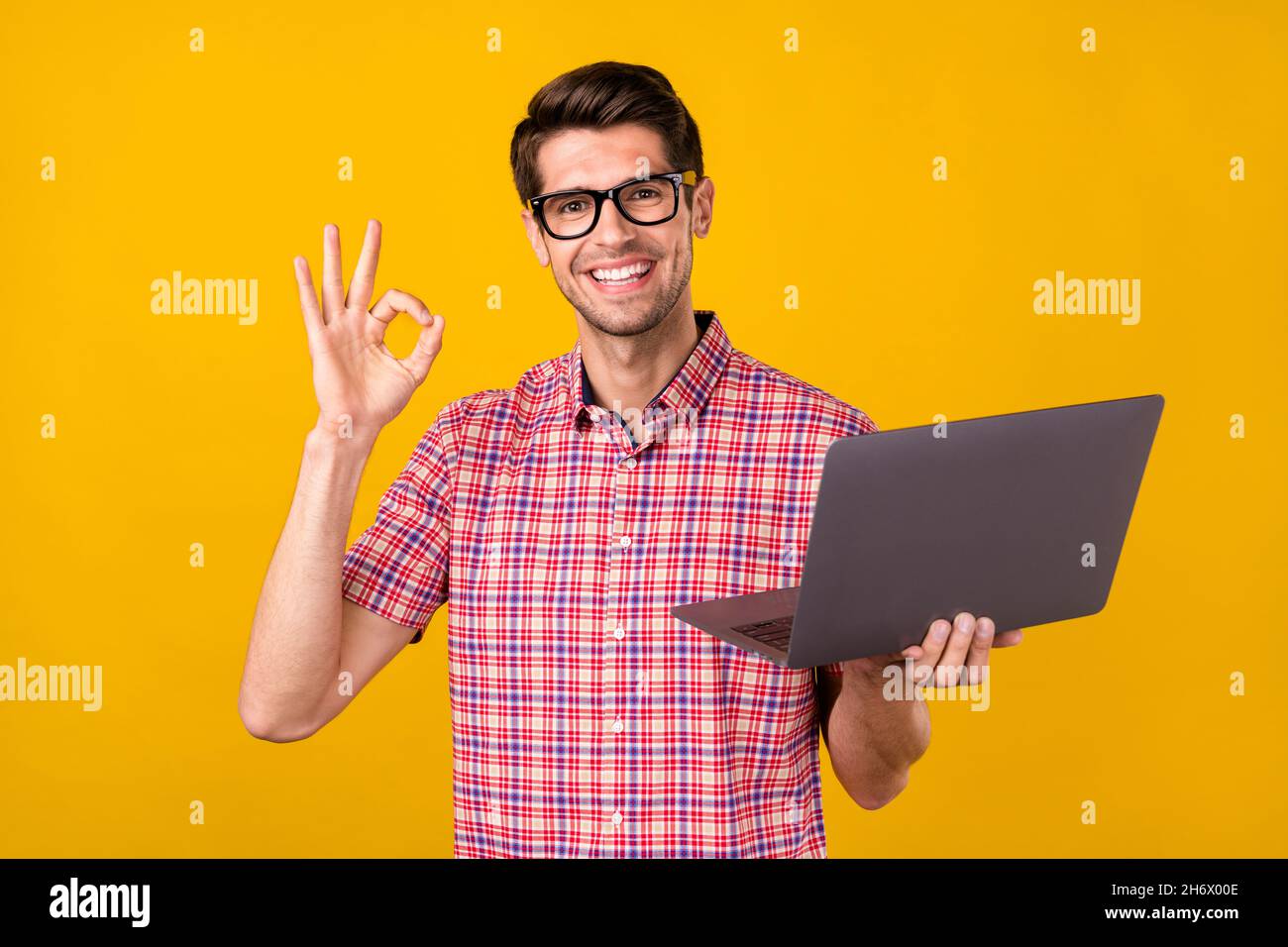 Portrait of attractive trendy cheerful guy geek using laptop showing ok ...