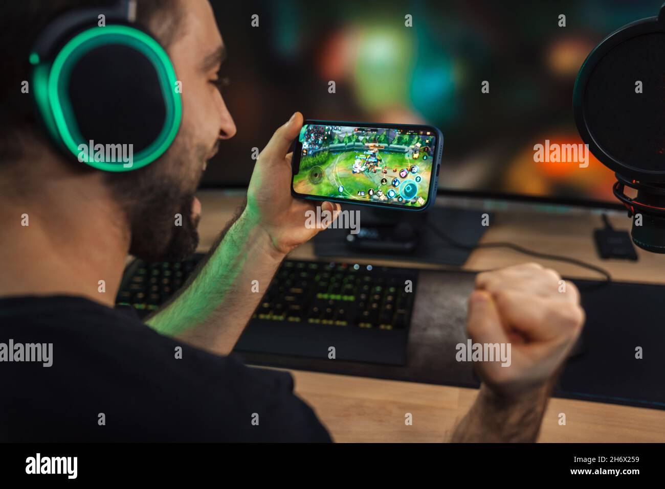 Young man gamer playing video games on smartphone and computer in dark ...