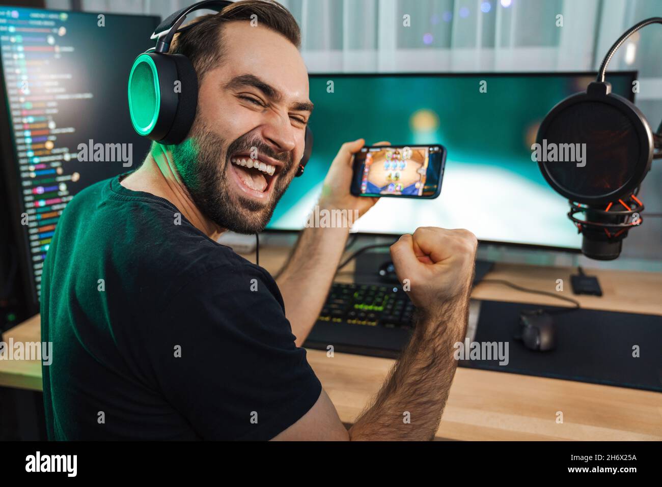 Young man gamer playing video games on smartphone and computer in dark ...