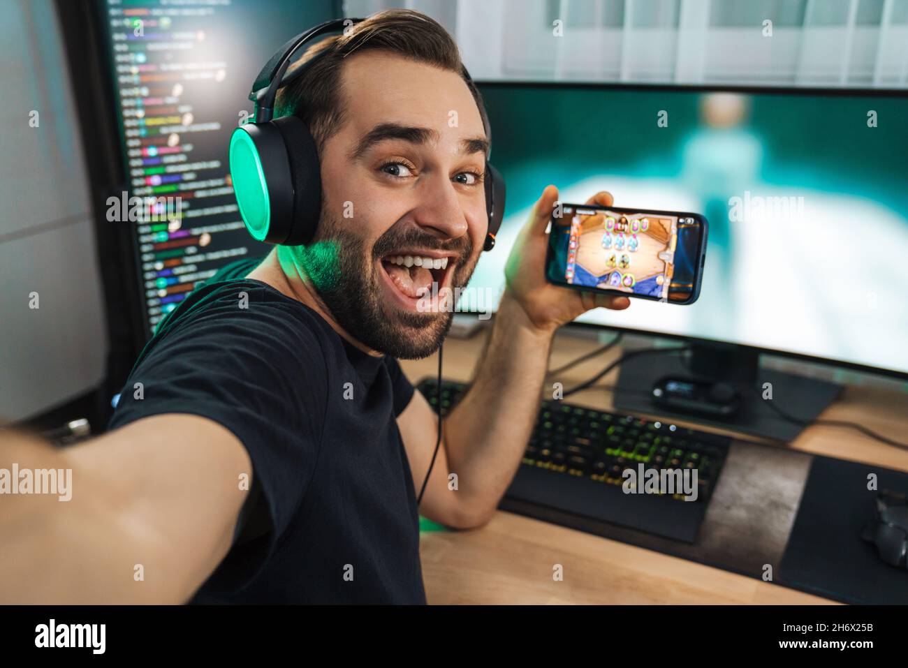 Young man gamer playing video games on smartphone and computer in dark ...