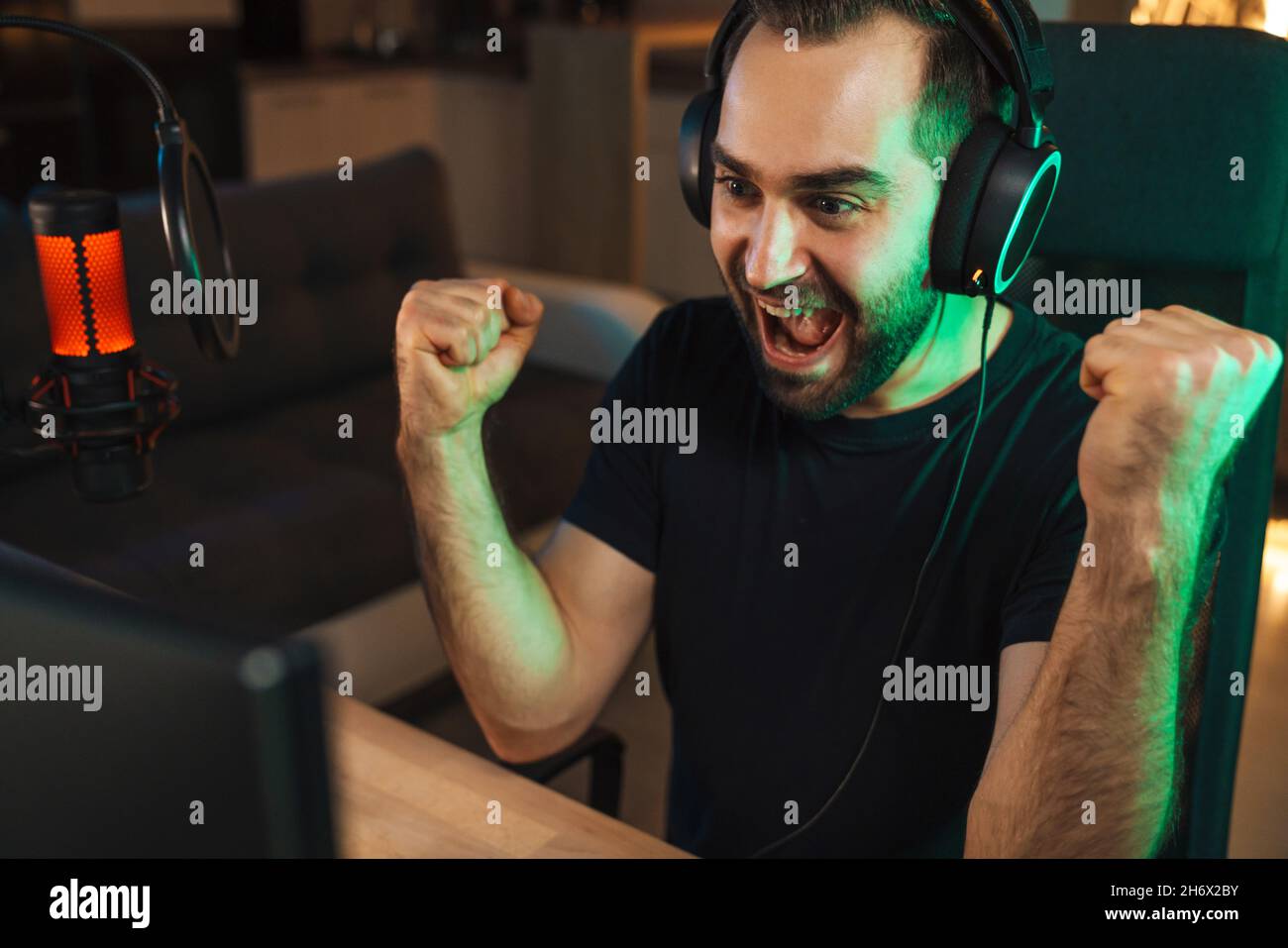 Happy young man gamer streamer in headphones playing on computer ...