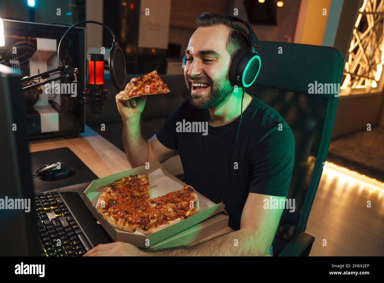 Happy young man in headset with pc computer eating pizza while playing ...