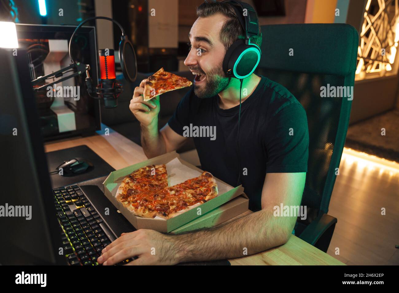 Happy young man in headset with pc computer eating pizza while playing ...