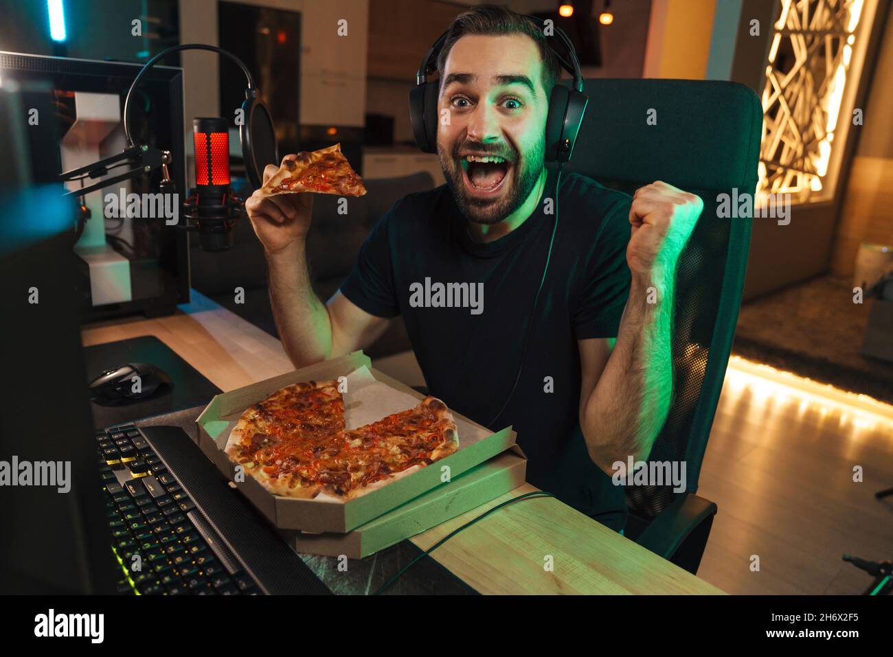 Happy young man in headset with pc computer eating pizza while playing ...
